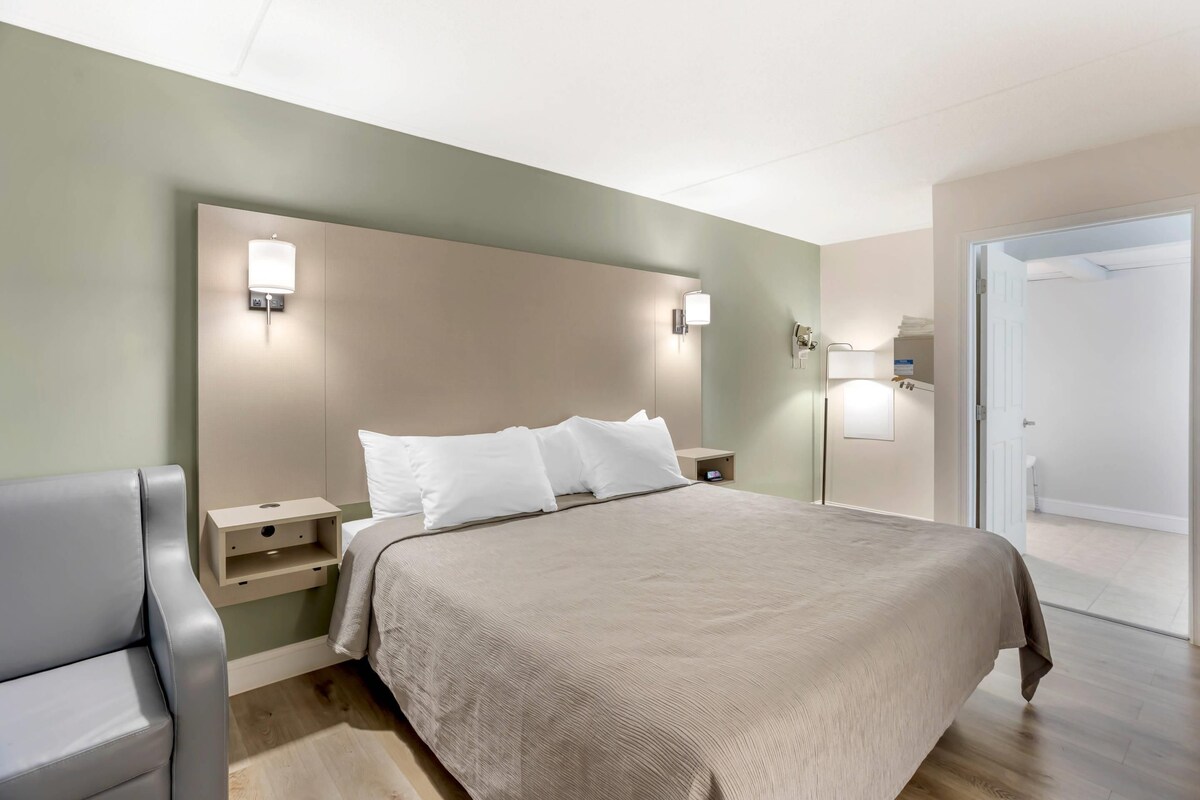 Quarto de hotel moderno com uma cama grande, mesas de cabeceira e iluminação embutida na parede.