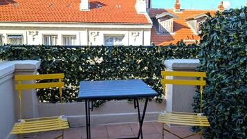 Um terraço com uma mesa e duas cadeiras amarelas, cercado por um viveiro e edifícios com telhados vermelhos.