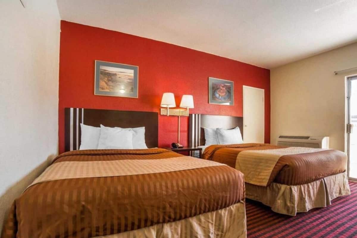 Quarto de hotel com duas camas, paredes vermelhas e chão quadriculado.