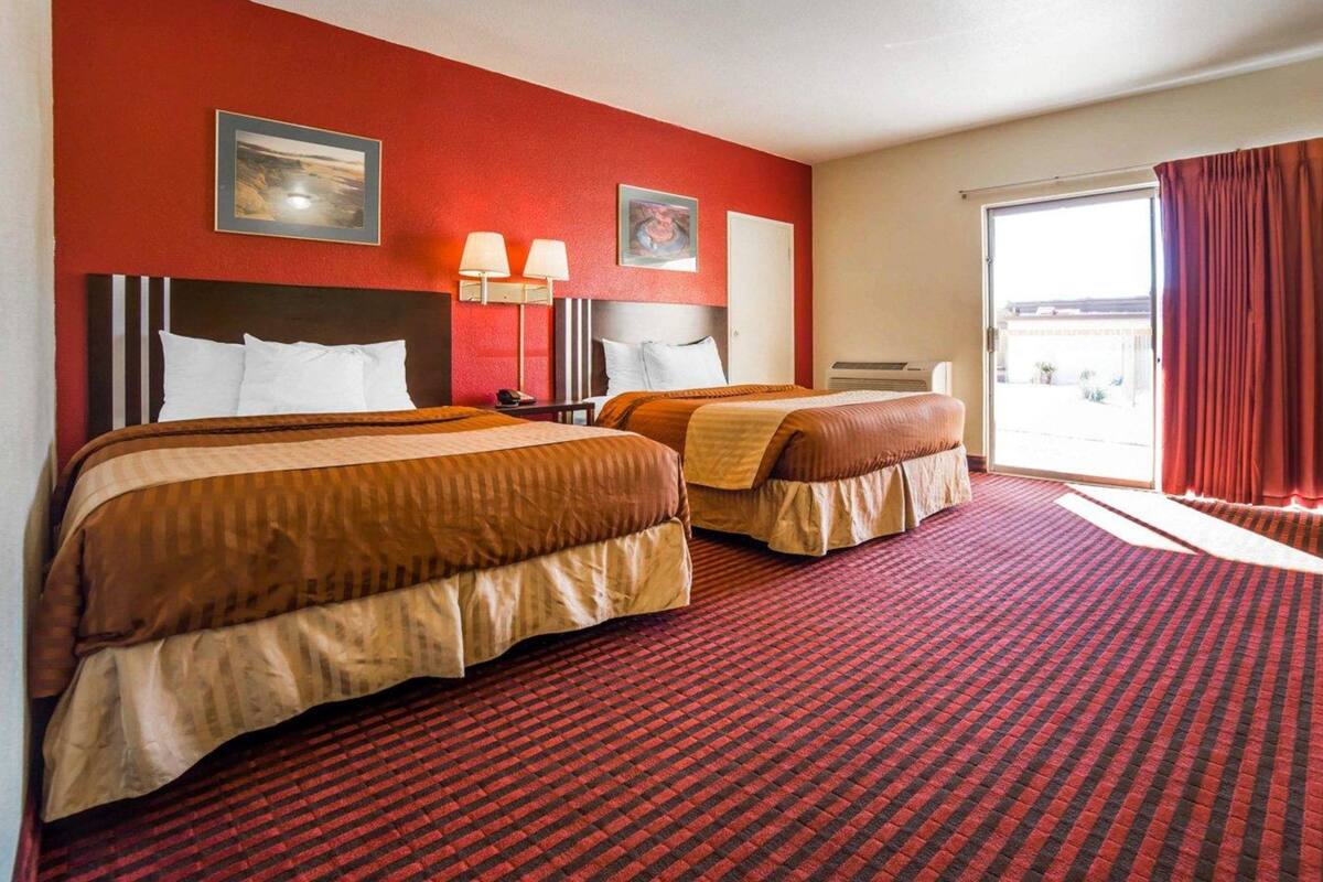 Quarto de hotel com duas camas, paredes vermelhas e tapete vermelho.