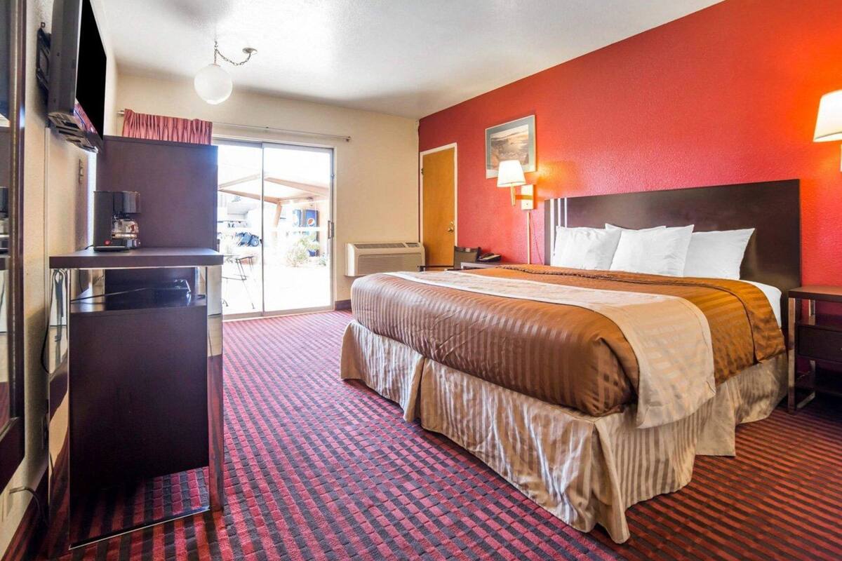 Quarto de hotel com cama, escrivaninha, televisão e janela.