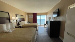 Quarto de hotel com duas camas, uma escrivaninha, uma cadeira, televisão e vista para o mar.