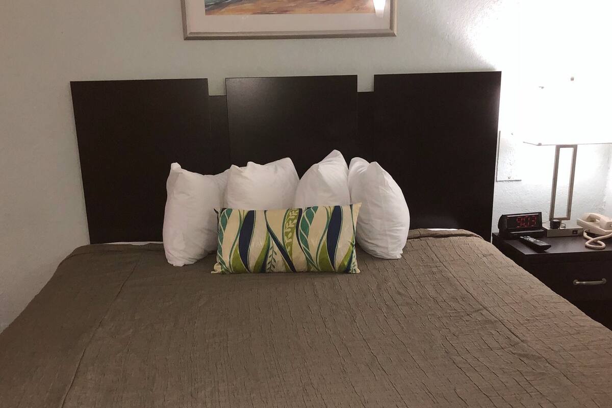 Uma cama com colcha marrom, um travesseiro decorativo e cabeceira preta.
