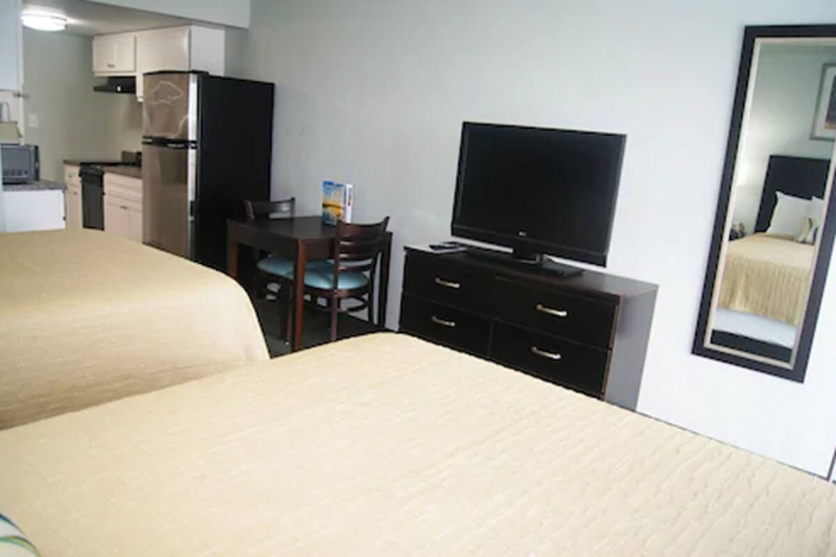 Quarto de hotel com duas camas, televisão, escrivaninha com cadeira, frigorífico e micro-ondas.