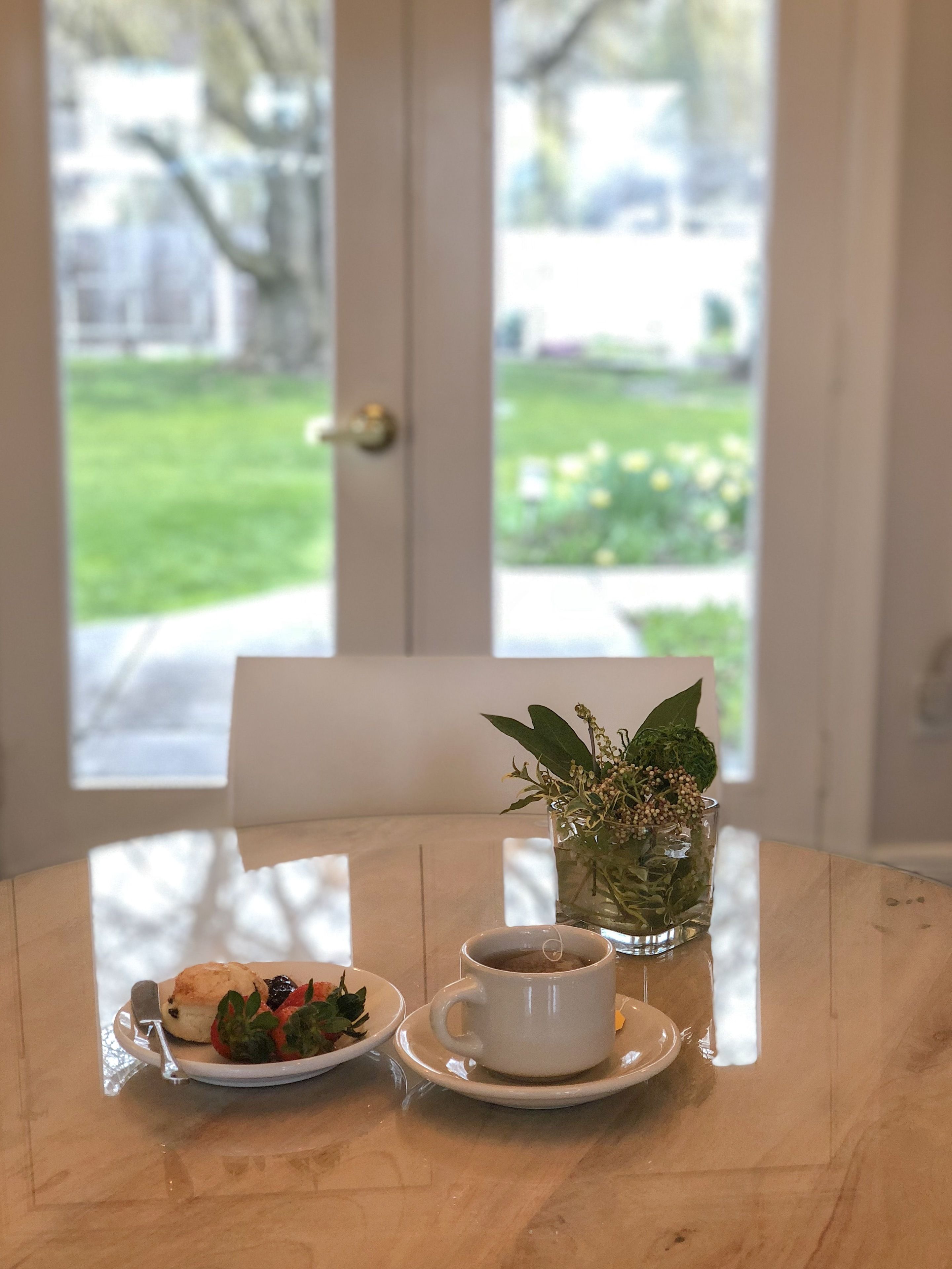 Uma mesa com um prato de comida, uma xícara de café, um copo de água e um vaso de flores.
