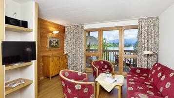 Um quarto aconchegante com um armário de madeira, uma televisão, um sofá vermelho e uma mesa com vista para montanhas através de grandes janelas.