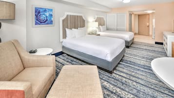 Quarto de hotel com duas camas, um sofá, uma mesinha, uma luminária e um quadro na parede.