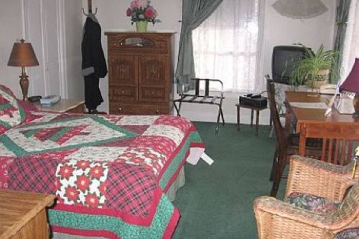 Quarto com cama, cômoda de madeira, televisão, cadeira e escrivaninha com abajur.