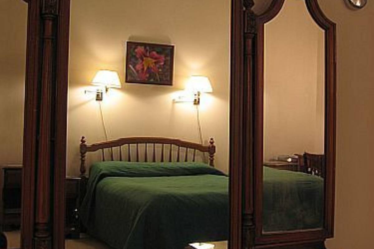 Quarto com cama de madeira, duas luminárias de cabeceira, um quadro na parede e um espelho na parede.
