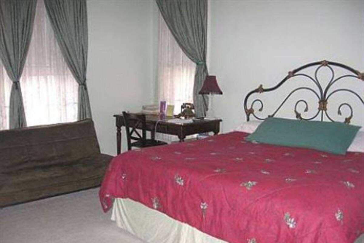 Quarto com cama, mesa de cabeceira, luminária e janela com cortinas.