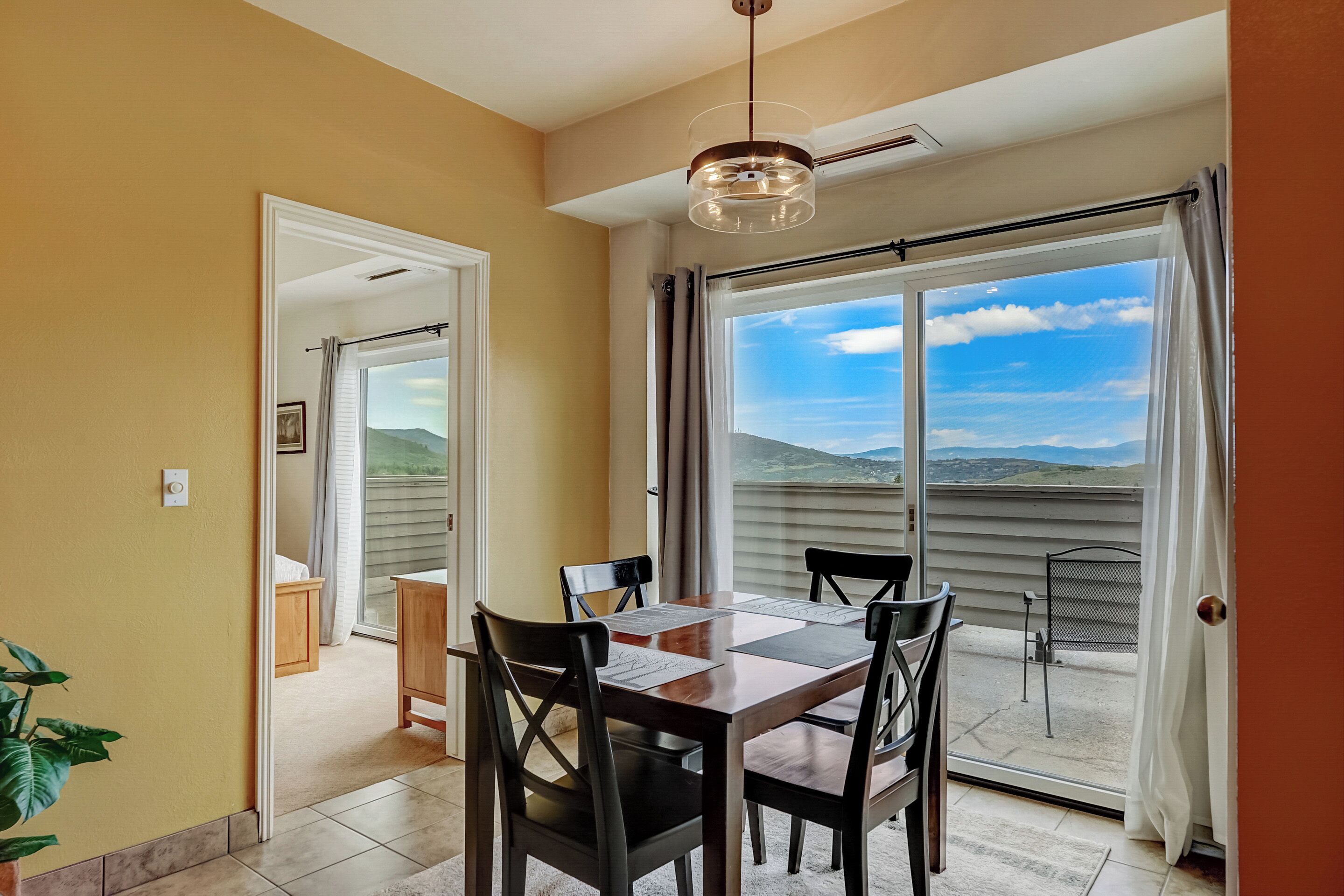 Uma área de jantar com mesa e cadeiras, uma luminária no teto e vista para uma varanda através de uma porta de correr de vidro.