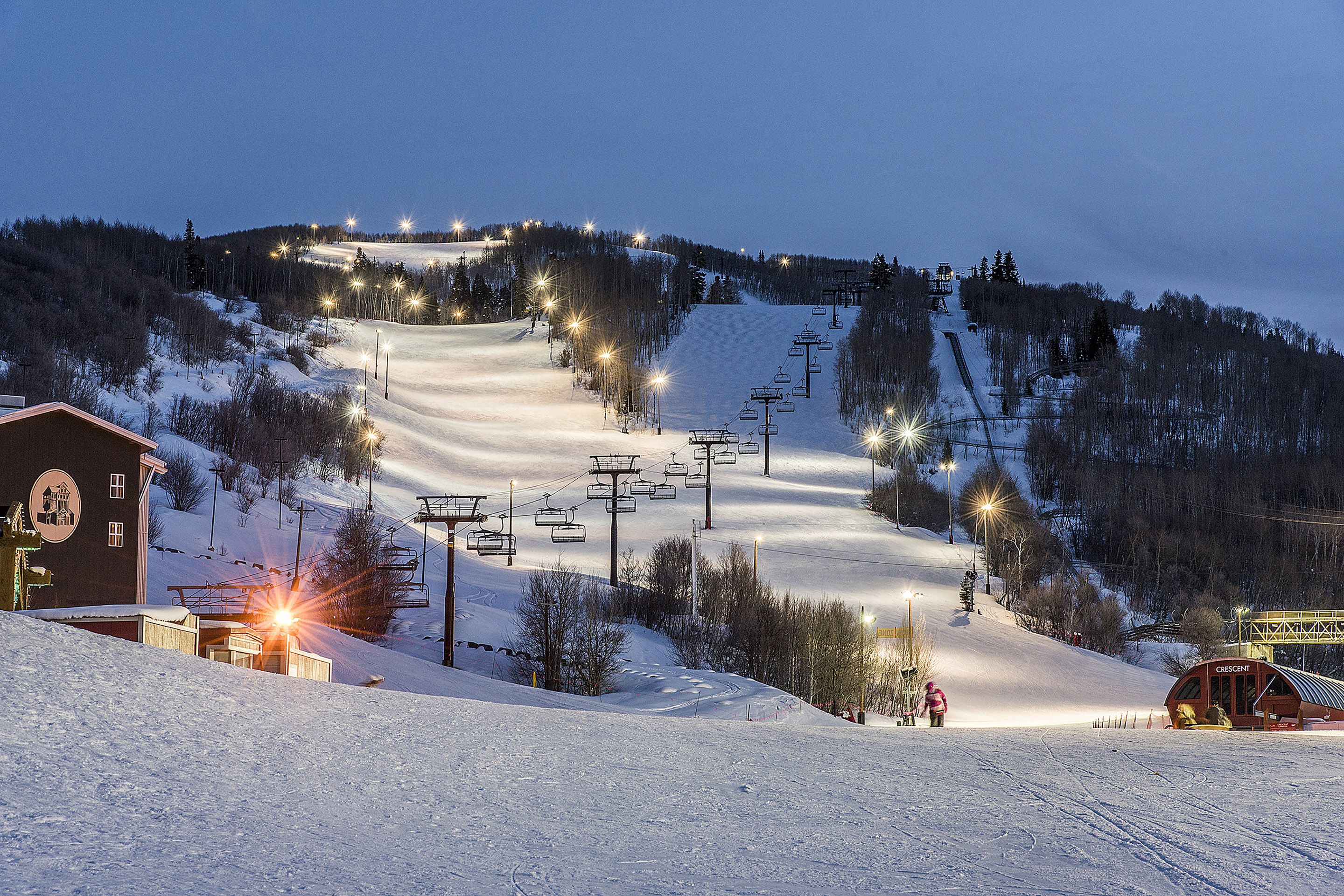 Pista de esqui coberta de neve com um teleférico e um chalé na base.