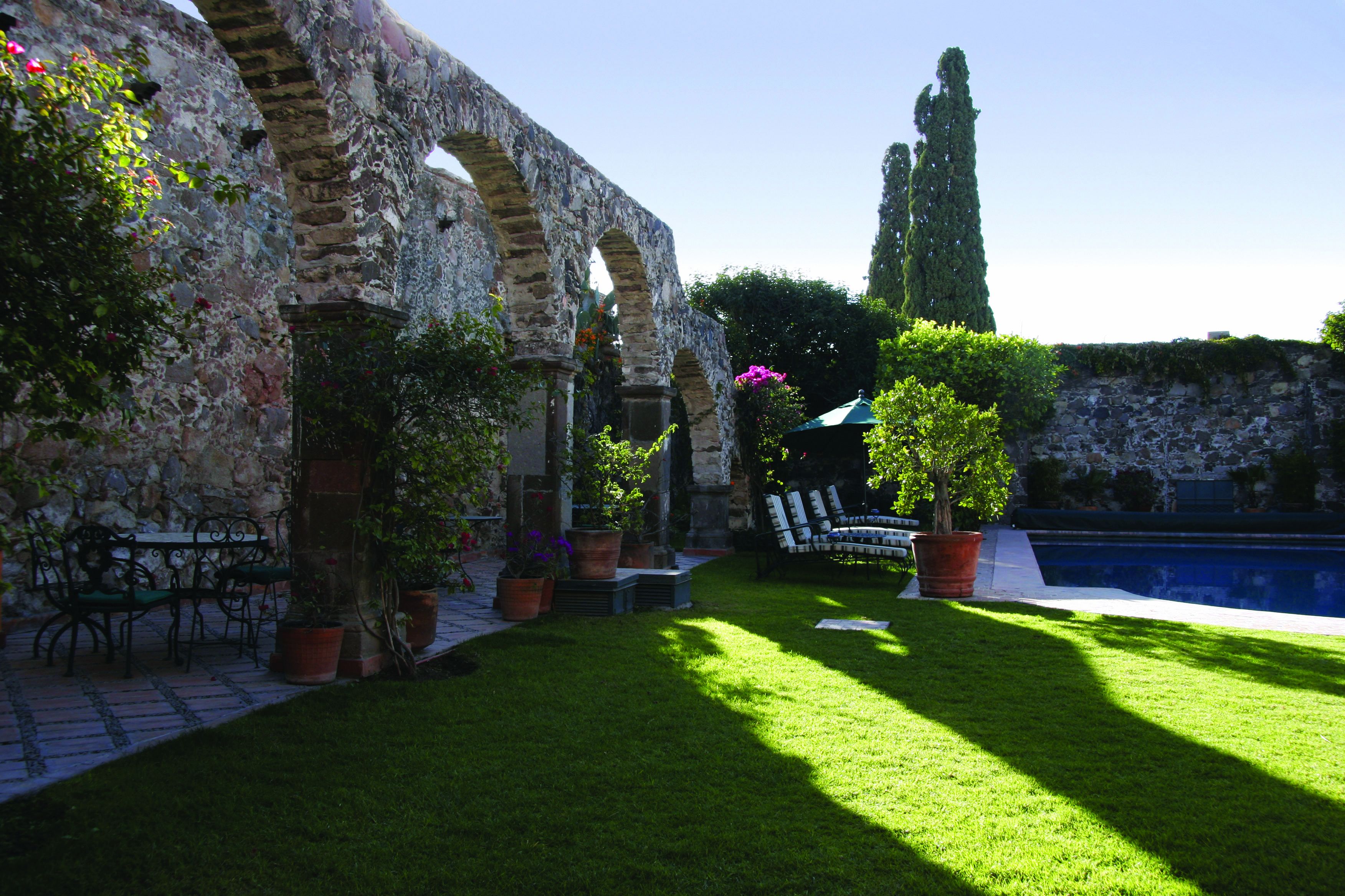 Um pátio com arco de pedra, piscina e plantas em vasos.