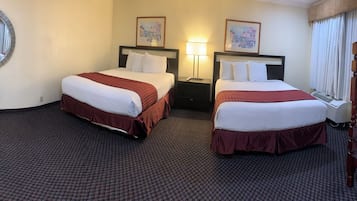 Quarto de hotel com duas camas de solteiro, uma escrivaninha com cadeira, um espelho grande e banheiro com banheira e chuveiro.