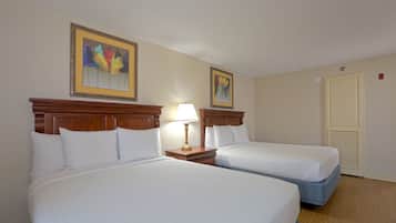 Quarto de hotel com duas camas, cabeceiras de madeira, roupa de cama branca e dois quadros florais emoldurados nas paredes.