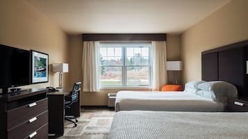 Quarto de hotel com duas camas, uma mesa com computador, televisão e janela com cortinas.