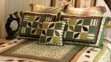 Uma cama com colcha e almofadas, quadros nas paredes e um espelho decorativo.