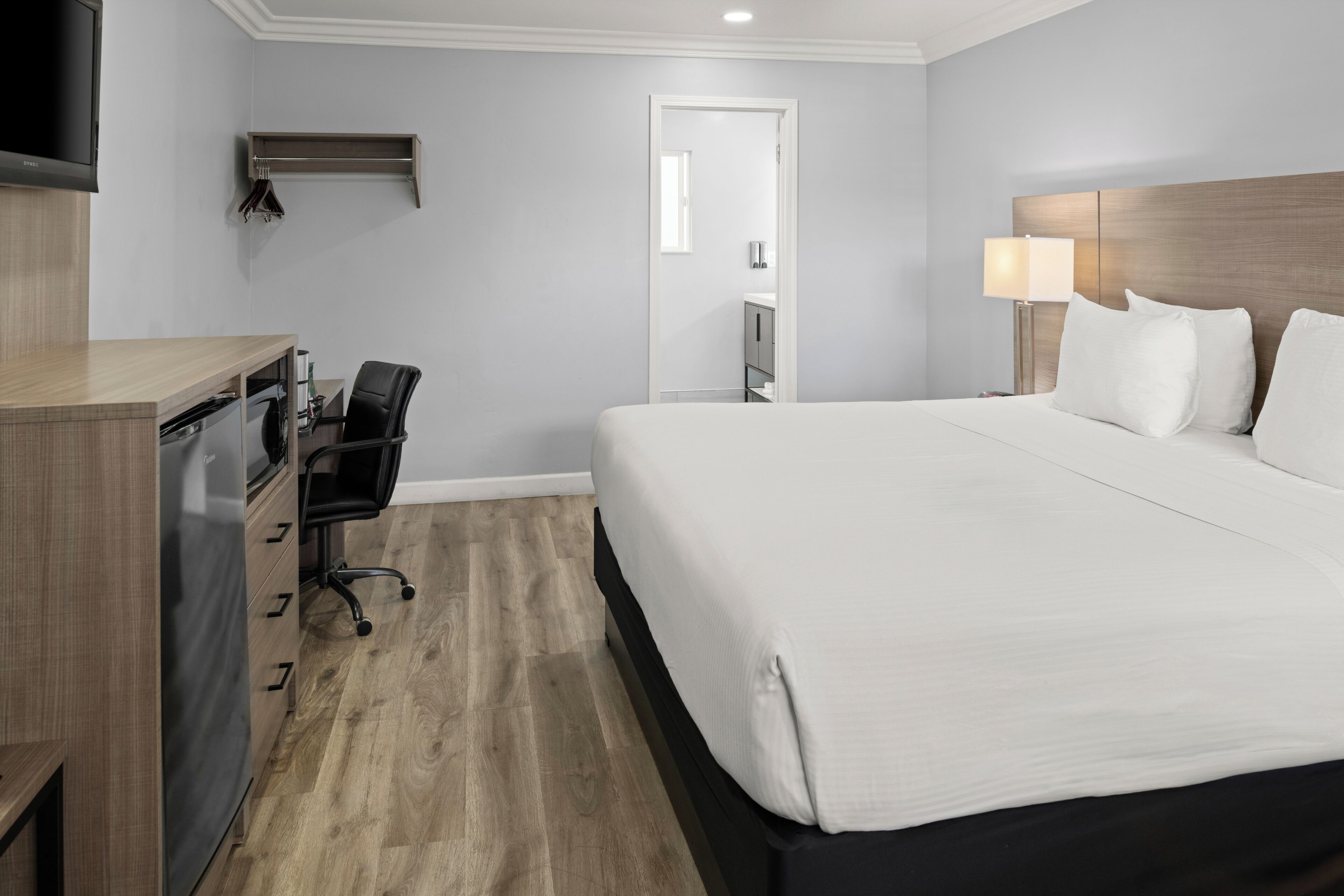 Quarto de hotel com cama, escrivaninha, cadeira e televisão.