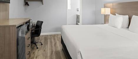 Quarto de hotel com cama, escrivaninha, cadeira e televisão.