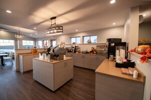 Cozinha moderna com armários de madeira, uma ilha central e área de refeições com vista para o exterior.