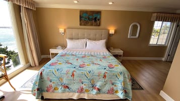 Quarto com uma cama grande, duas mesas de cabeceira, encosto da cama, um quadro e vista para o exterior.