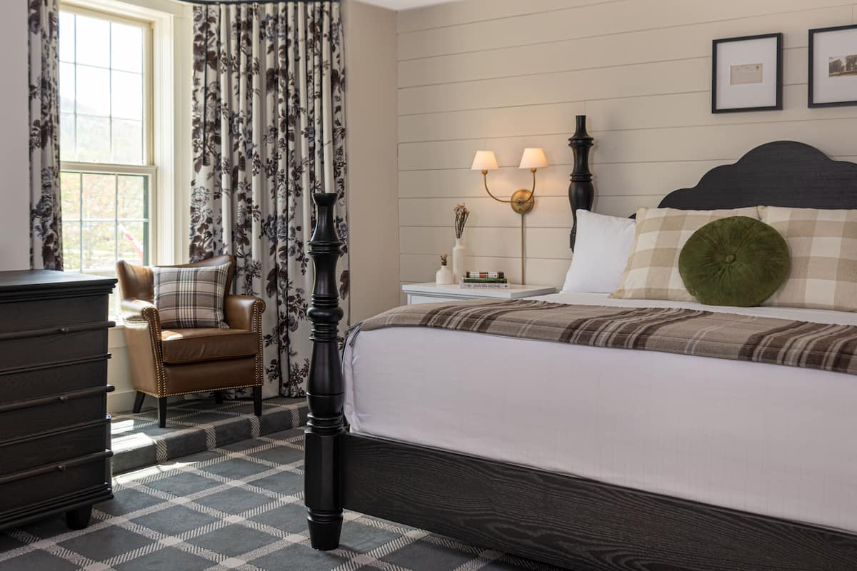 Quarto com cama, cômoda, cadeira, mesa de cabeceira e janela com cortinas.