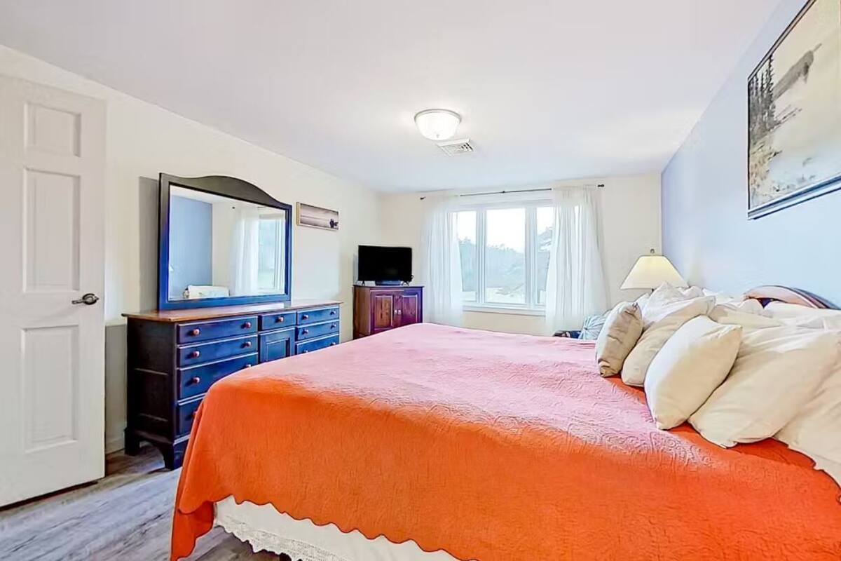 Quarto com uma cama grande, cômoda, televisão e janela com cortinas.