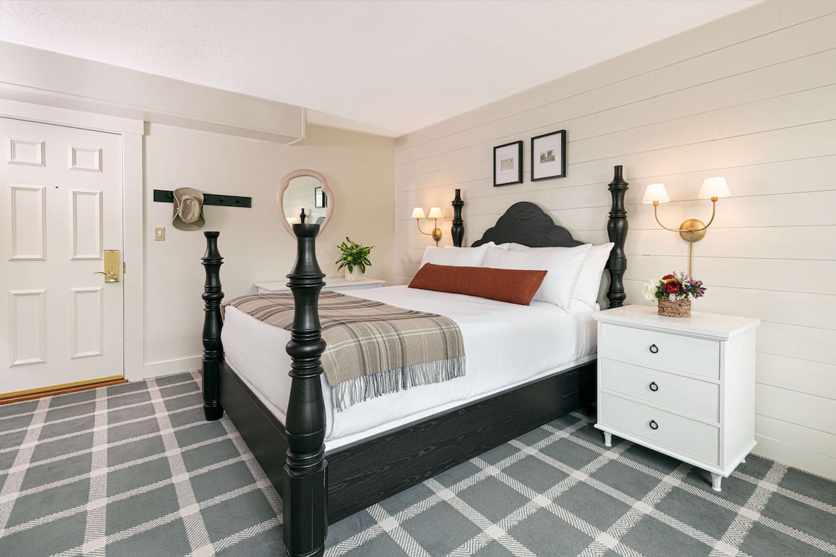 Quarto com cama, mesa de cabeceira, abajur e porta.