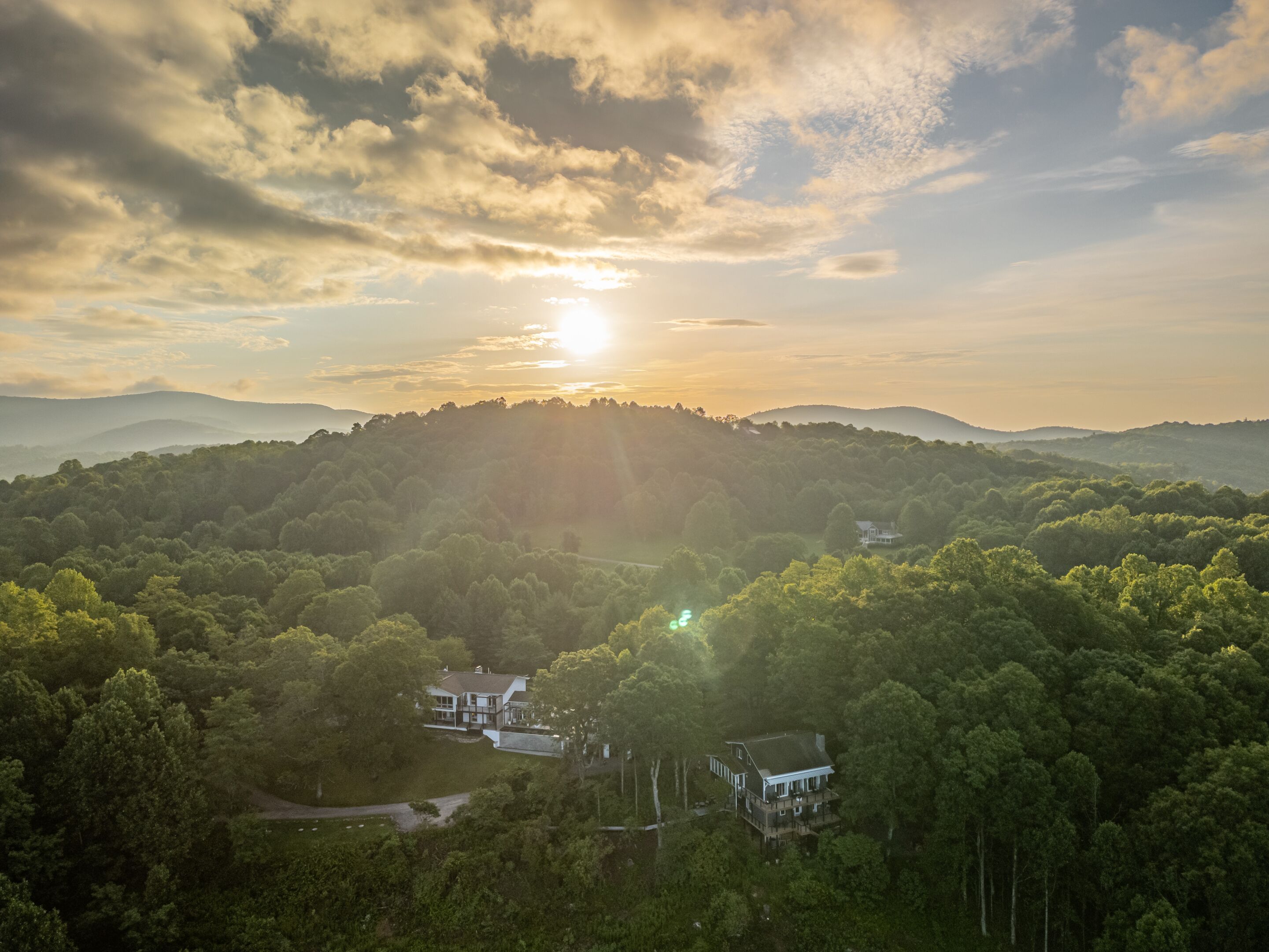 Uma casa cercada por mata densa, com vista desobstruída para o pôr do sol ao fundo.