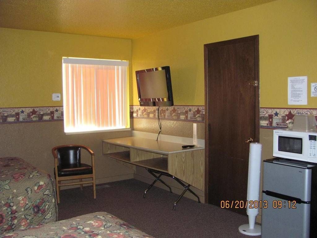 Quarto de hotel pequeno com uma cama de solteiro, uma mesa, uma cadeira, uma televisão e um micro-ondas.