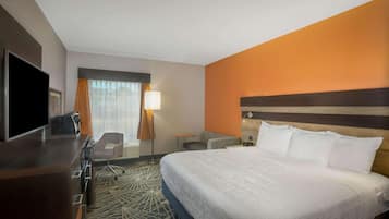 Quarto de hotel com uma cama grande, uma escrivaninha com televisão de tela plana, uma cadeira e uma mesinha.