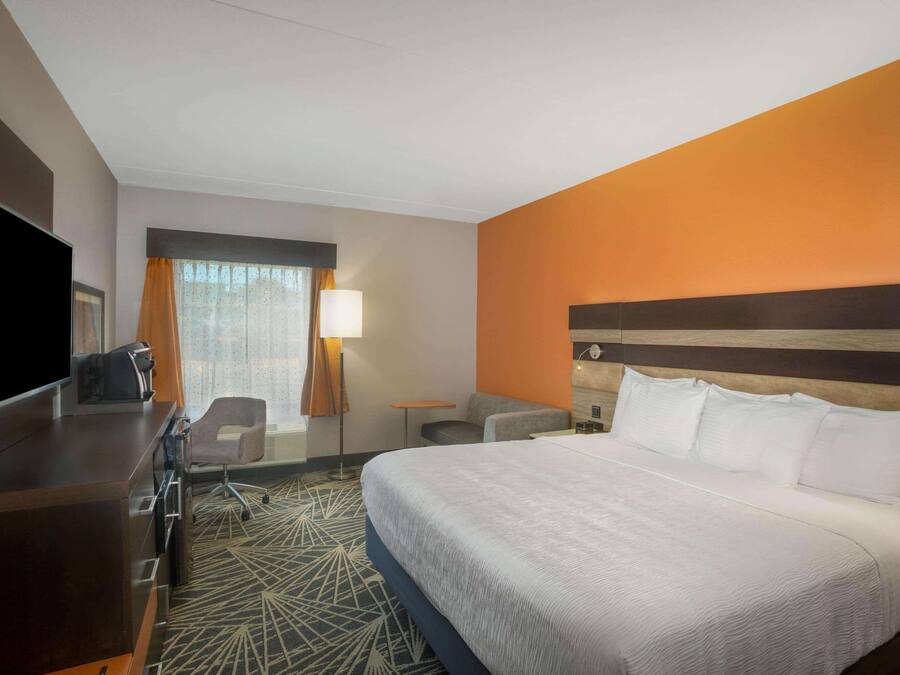 Quarto de hotel com uma cama grande, uma escrivaninha com televisão de tela plana, uma cadeira e uma mesinha.