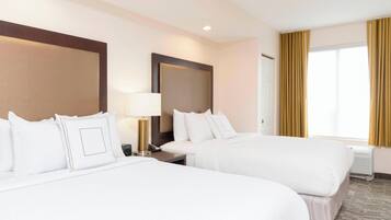 Quarto de hotel com duas camas, uma mesa de cabeceira, uma luminária, um espelho grande e uma janela com cortinas.