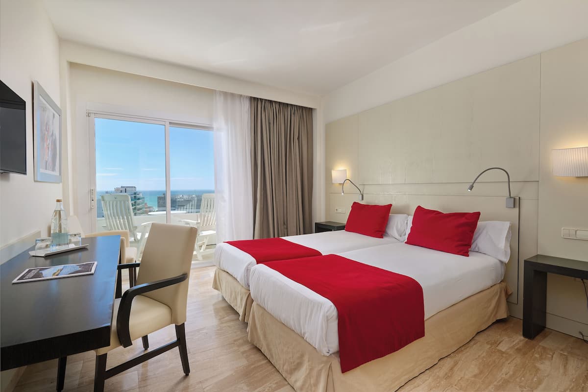Quarto de hotel com uma cama grande, uma escrivaninha e uma cadeira. Há uma janela com vista para a cidade.