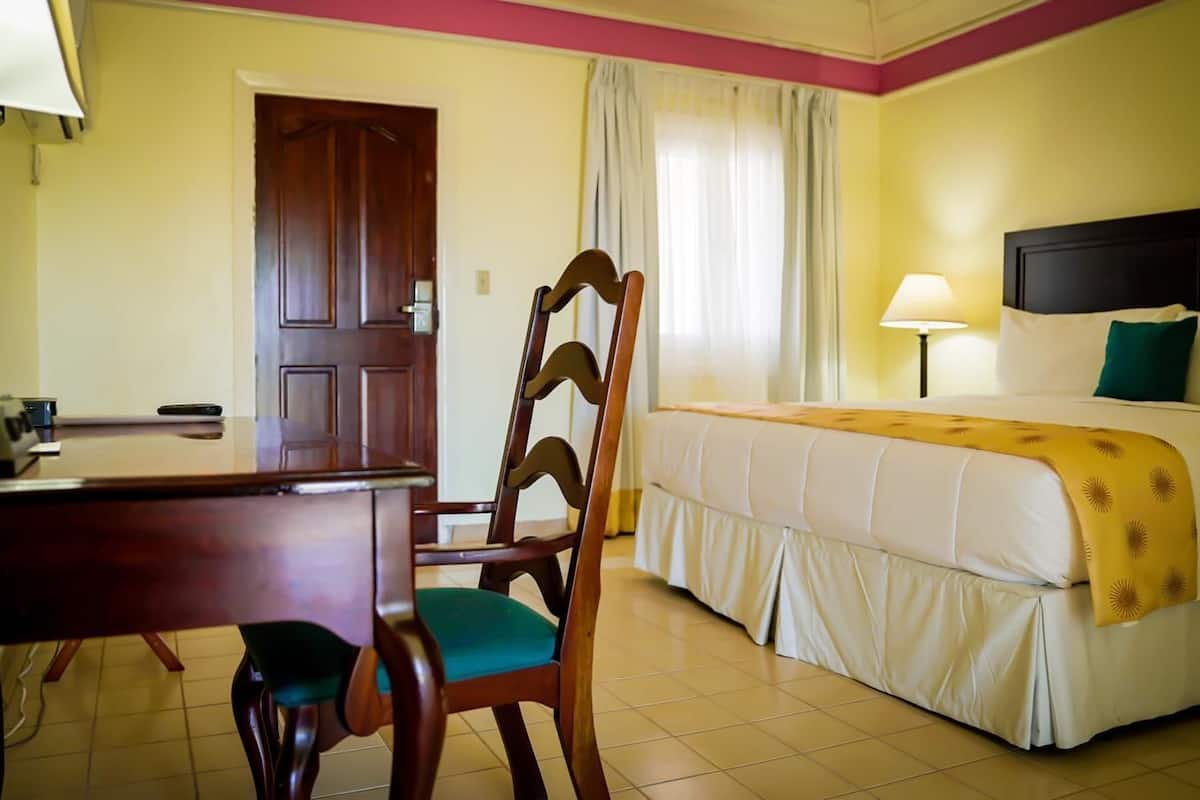 Quarto de hotel com cama, escrivaninha, cadeira e luminária.