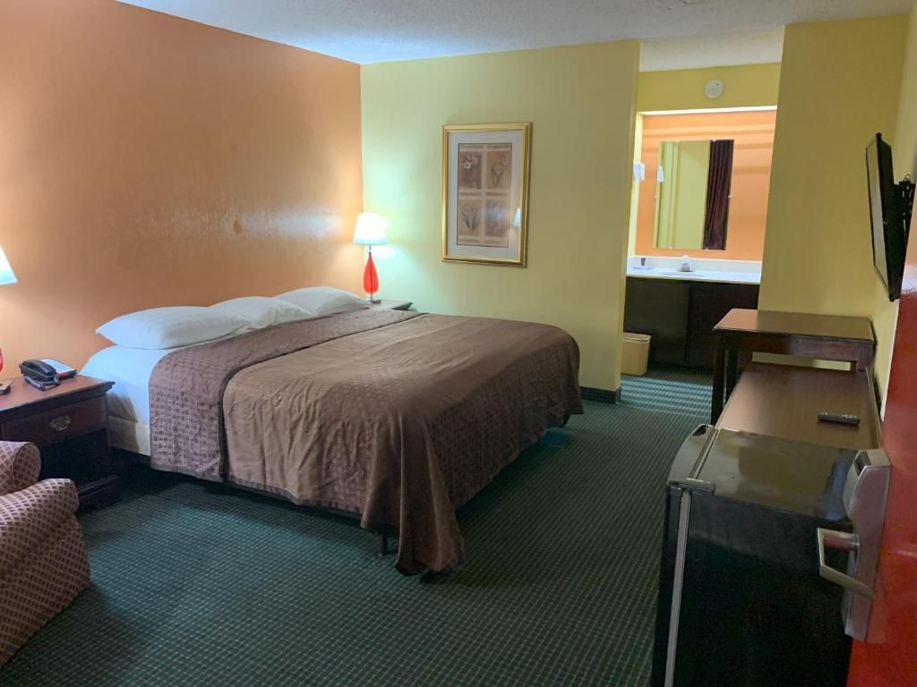 Quarto de hotel com cama, mesa de cabeceira, abajur, cadeira e escrivaninha com espelho.