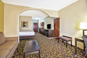 Quarto de hotel com cama, sofá, escrivaninha, televisão e porta que dá para outro espaço.