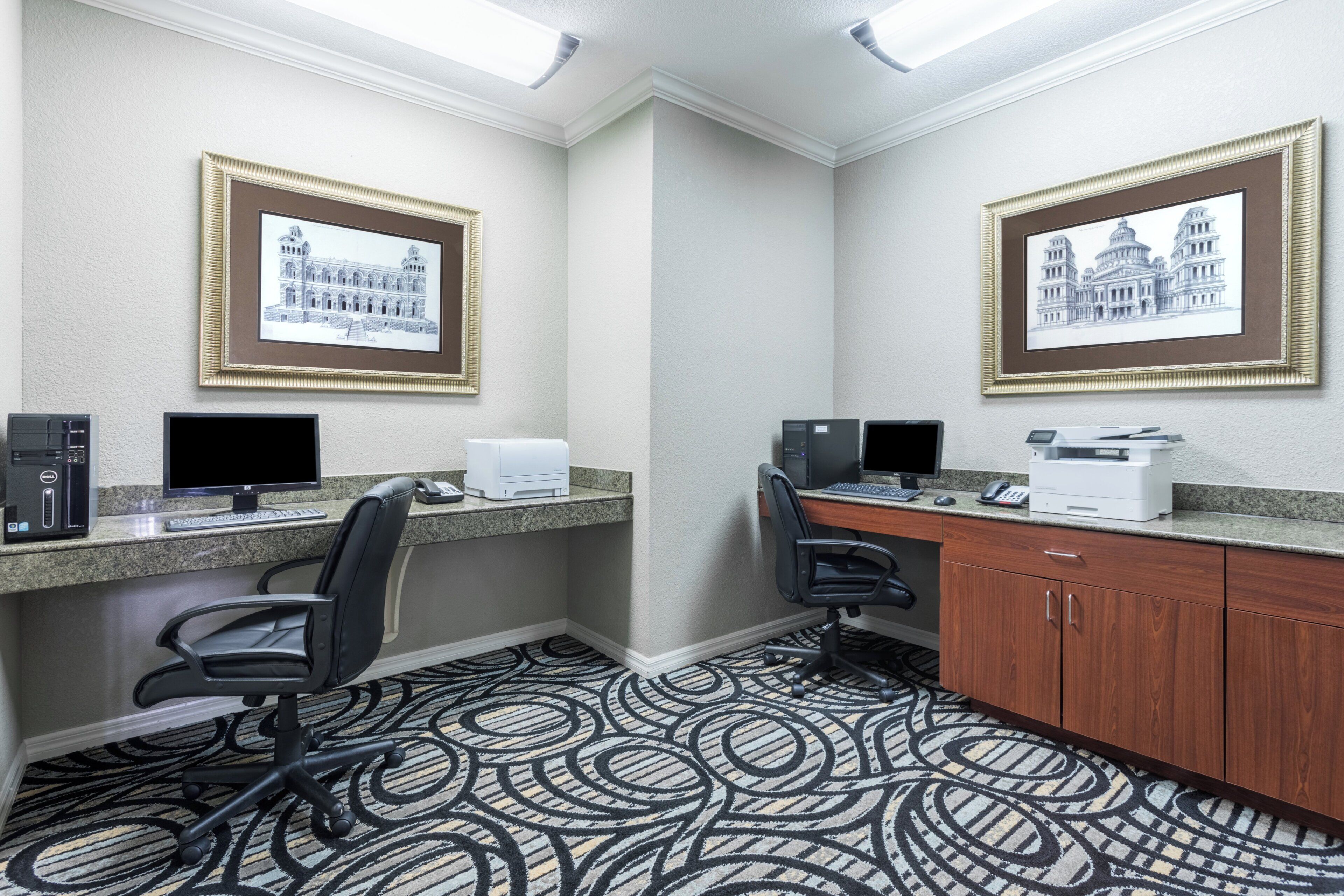 Quarto de hotel com duas mesas de trabalho, cada uma com computador, impressora e uma obra de arte emoldurada.