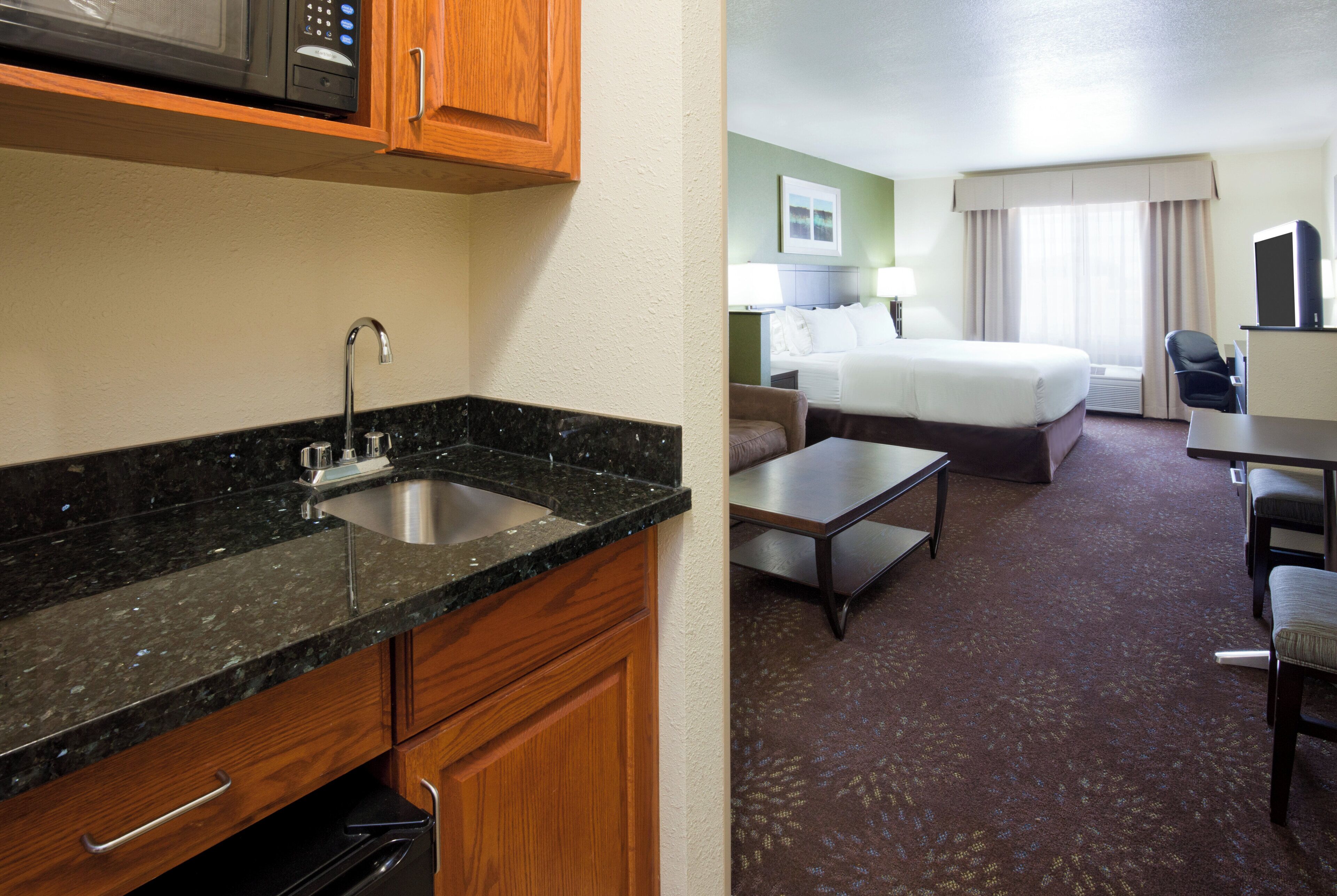 Quarto de hotel com cozinha compacta, cama, escrivaninha e televisão.