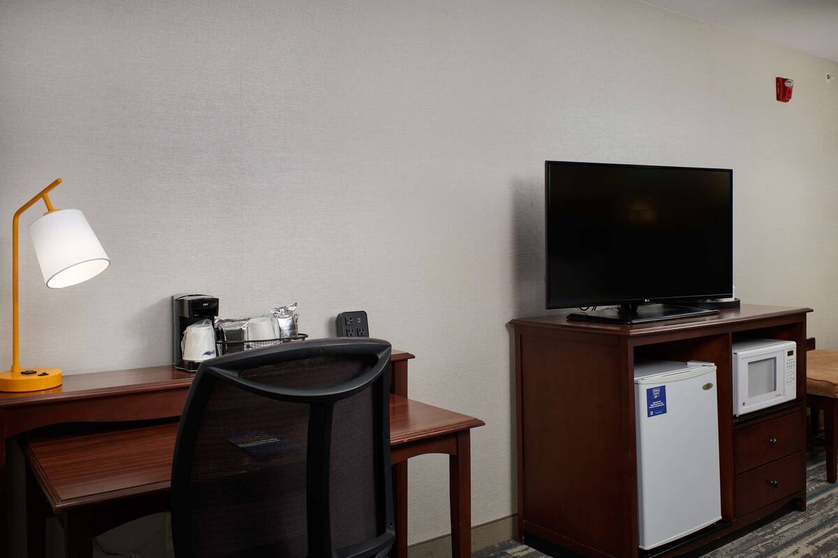 Quarto de hotel com uma escrivaninha de madeira, televisão sobre suporte, micro-ondas e frigorífico.