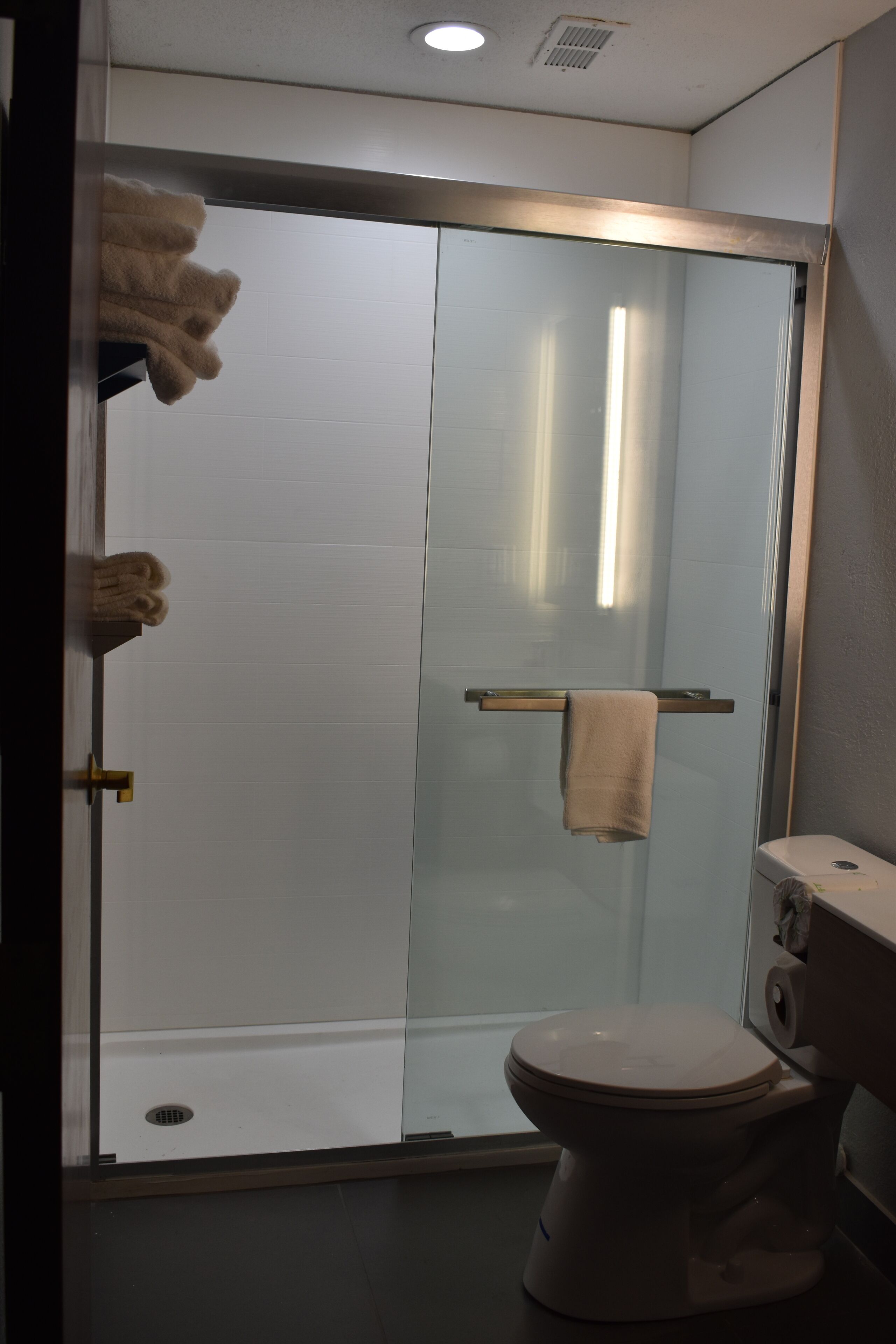 Uma casa de banho moderna com cabine de chuveiro em vidro, sanita e um porta-toalhas com toalhas.