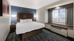 Quarto de hotel com uma cama grande, mesa de cabeceira, luminária fixada na parede, janela com cortinas e ar-condicionado na parede.