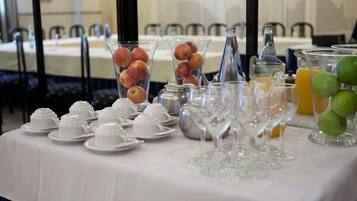 Mesa posta com copos de vidro transparente, bules brancos e frutas em jarras, sugerindo um buffet de café da manhã.