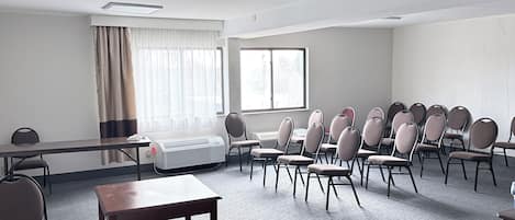 Uma sala de conferências com uma mesa comprida, várias cadeiras, uma janela com cortinas e uma luminária no teto.