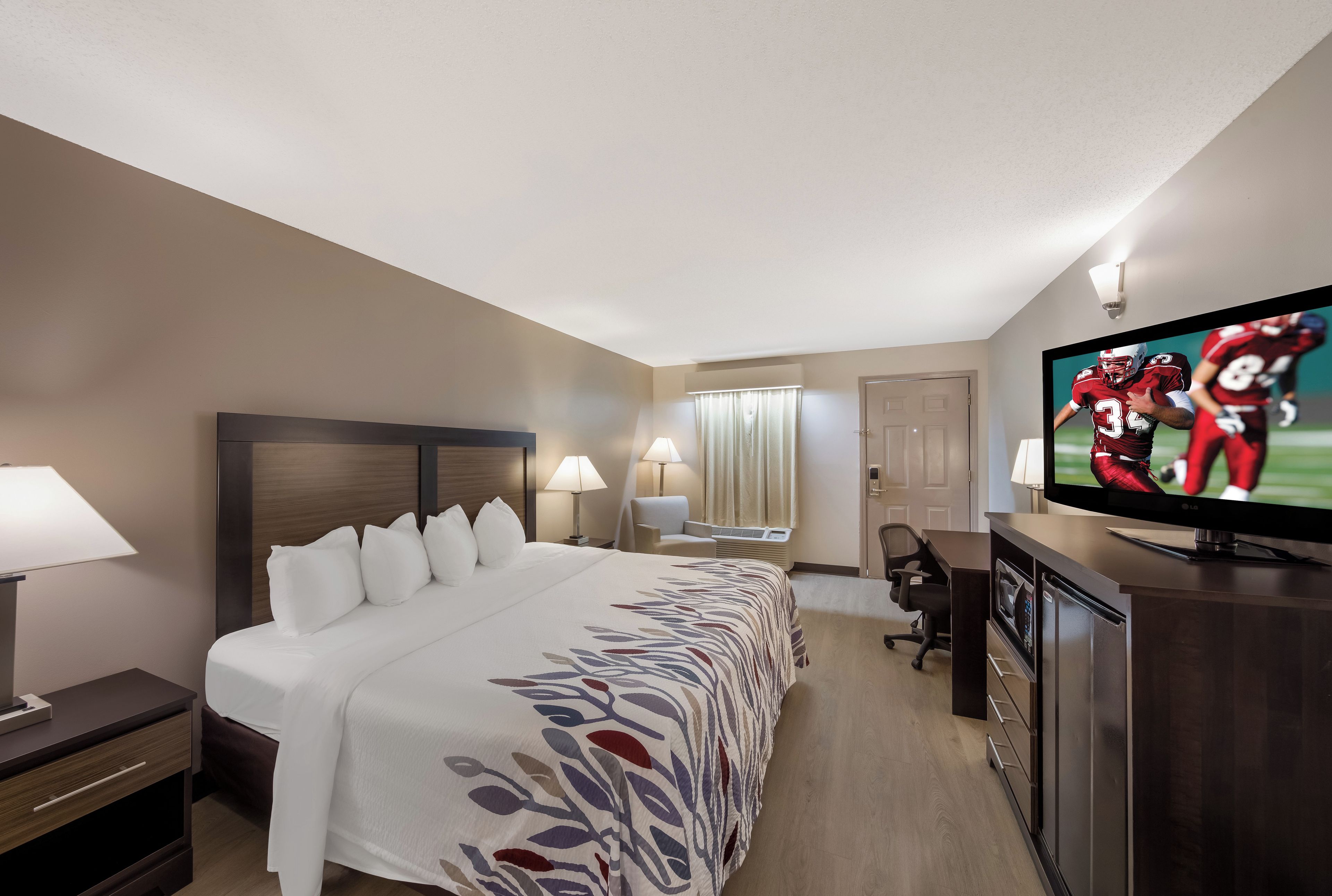 Quarto de hotel com uma cama grande, uma escrivaninha, uma televisão e uma janela com cortinas.