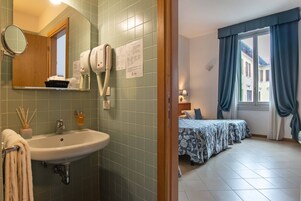 Casa de banho com lavatório, espelho e secador de cabelo, e quarto com cama e janela.
