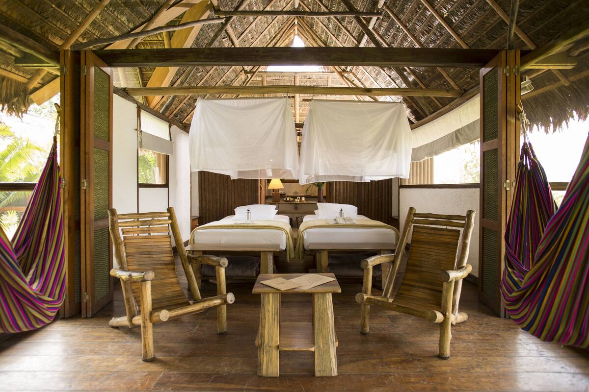 Quarto com duas camas, mobiliário de madeira e telhado de palha.