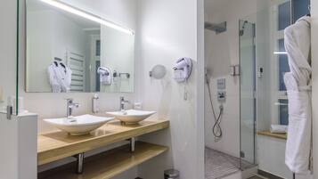 Um banheiro moderno com duas pias, um espelho grande, secador de cabelo e box de vidro.