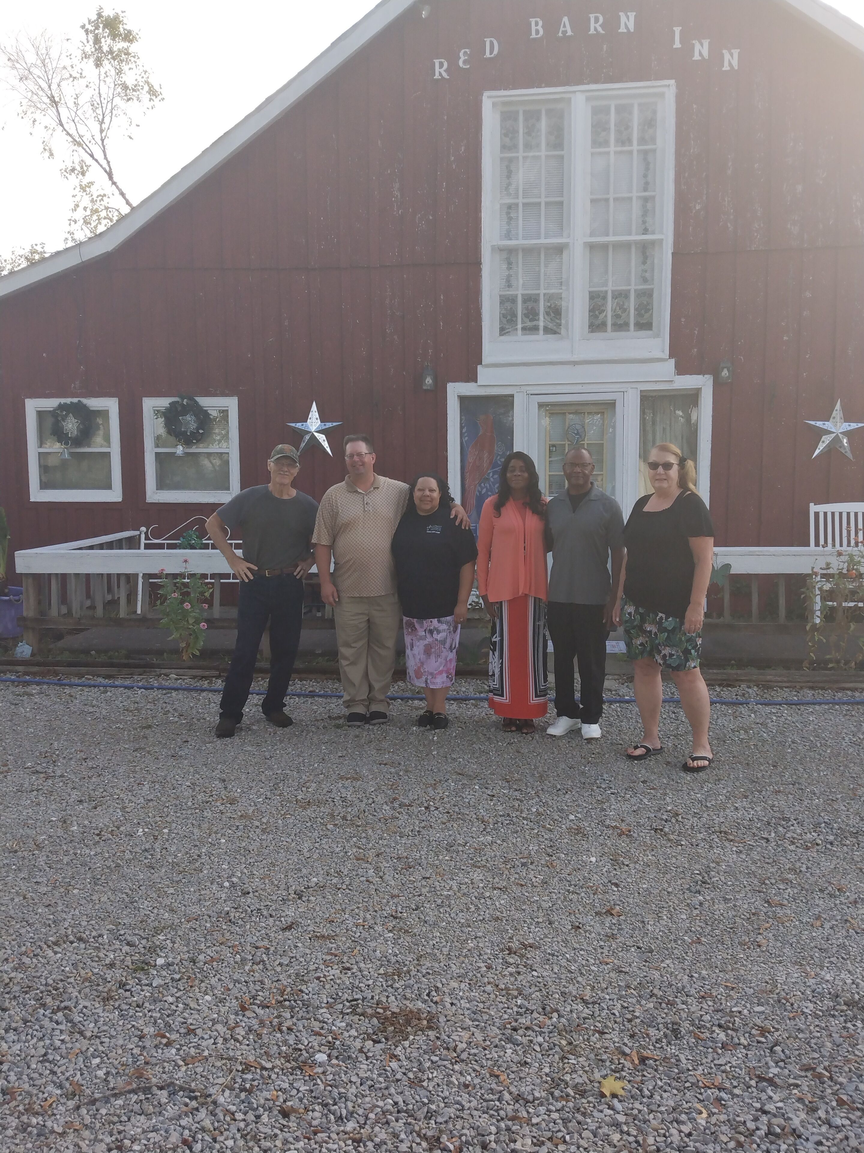 Um grupo de pessoas em frente a um prédio da Red Barn Inn, com uma grande janela e estrelas decorativas.