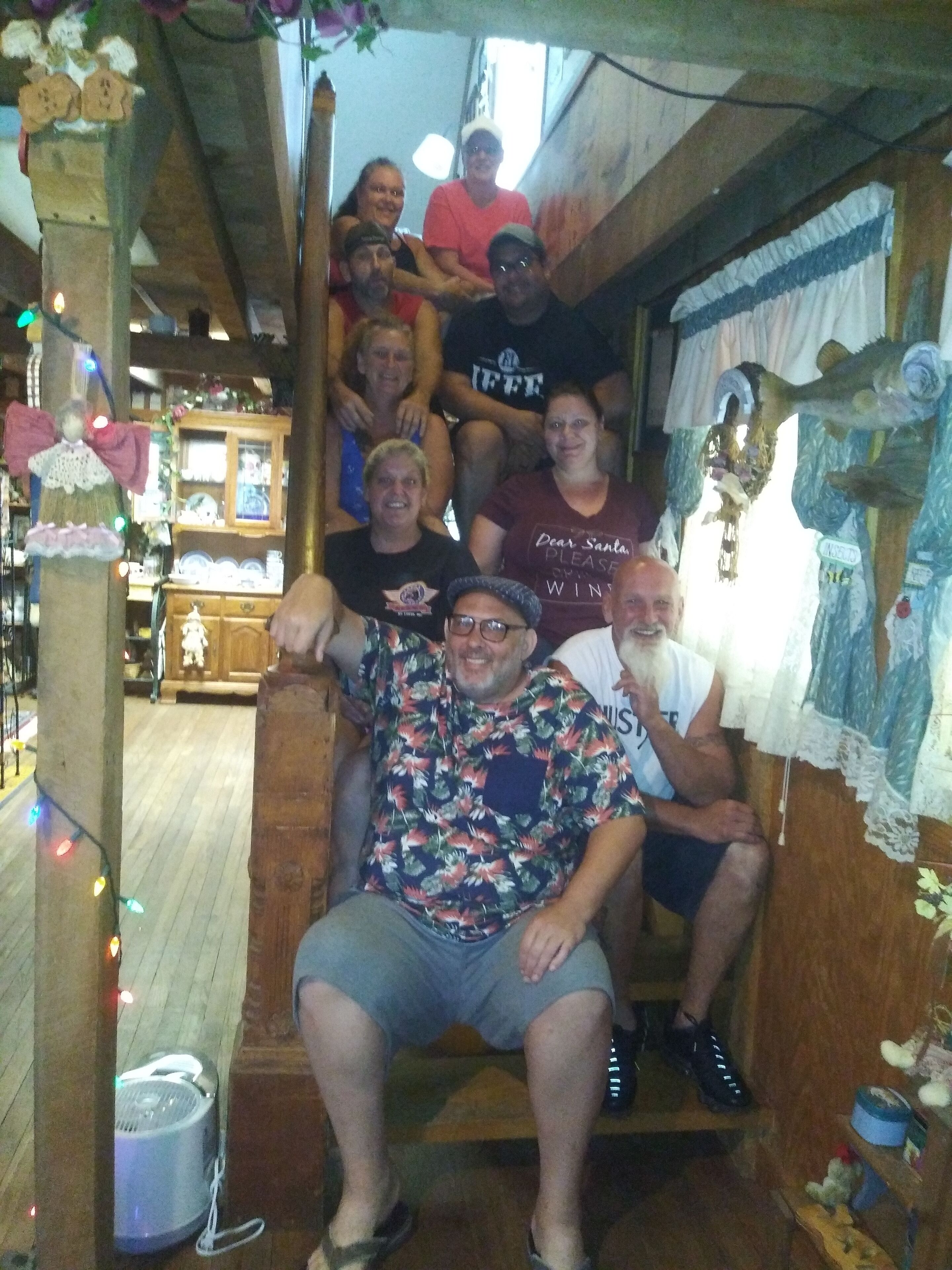 Um grupo de pessoas sentadas em um compartimento de madeira, com decoração rústica, incluindo chão de madeira e uma prateleira com diversos objetos.